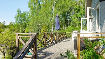 Um deck de madeira com guarda-corpo, que leva a um edifício com uma janela.