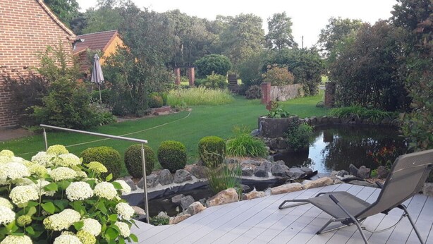 Um deck com uma cadeira, um lago e um jardim com hortênsias brancas.