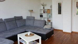 Uma sala de estar moderna com um sofá modular cinza, uma mesa de centro branca, uma estante e um relógio de parede.