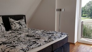 Quarto com cama, luminária de chão e vista para o exterior.