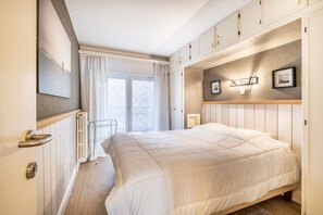 Quarto com cama, radiador, janela com cortinas e luminária fixada na parede.