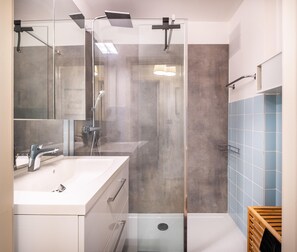 Uma casa de banho moderna com cabine de duche em vidro, lavatório branco e parede com azulejos azuis.