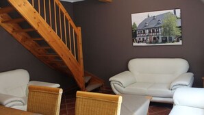 Quarto com escada de madeira, sofá de couro branco, cadeiras de vime e um quadro na parede.