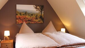 Quarto com uma cama grande, duas luminárias de cabeceira, um criado-mudo e um quadro de uma paisagem na parede.