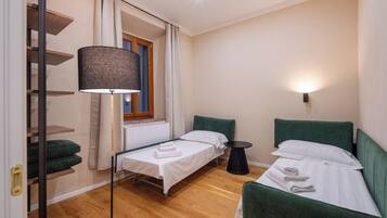 Um quarto pequeno e aconchegante com duas camas, um abajur e uma janela com cortinas.