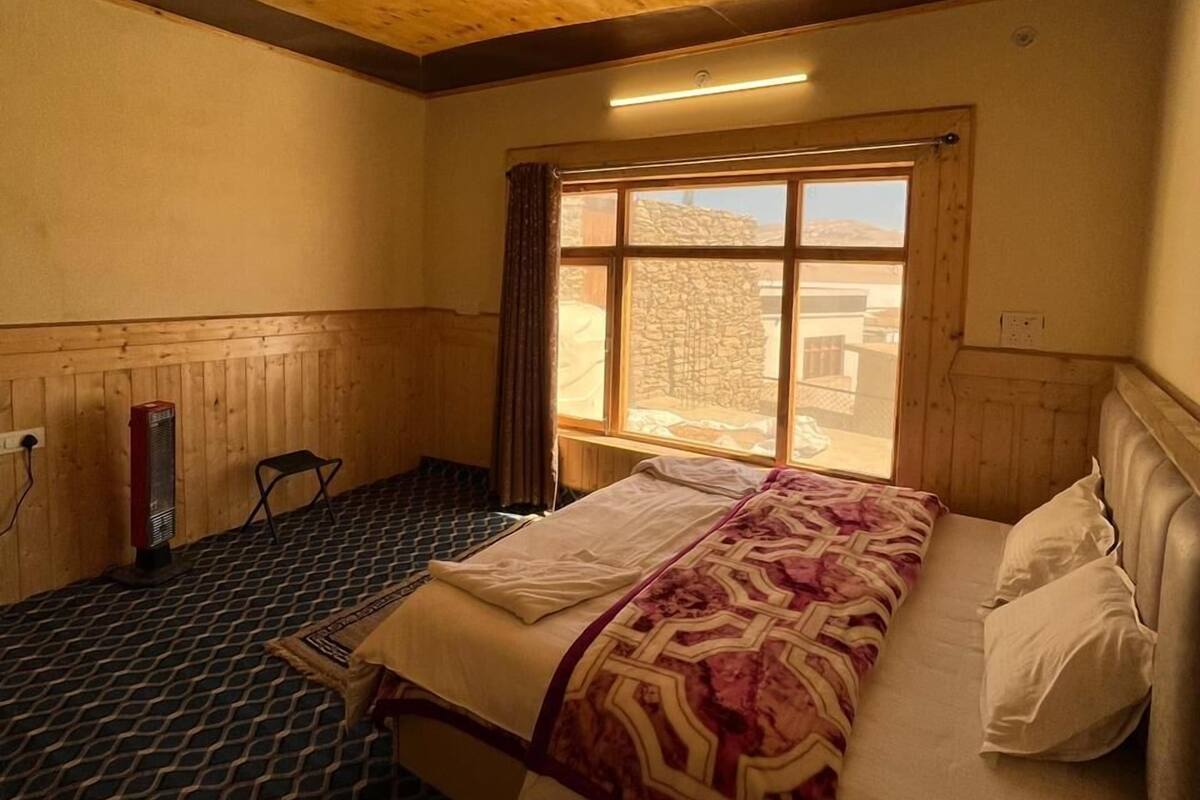 Quarto com teto de madeira, cama com manta estampada, aquecedor e janela com vista.