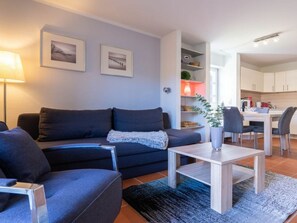 Uma sala de estar moderna com um sofá escuro, uma mesa de centro e uma área de jantar com cadeiras e uma mesa.