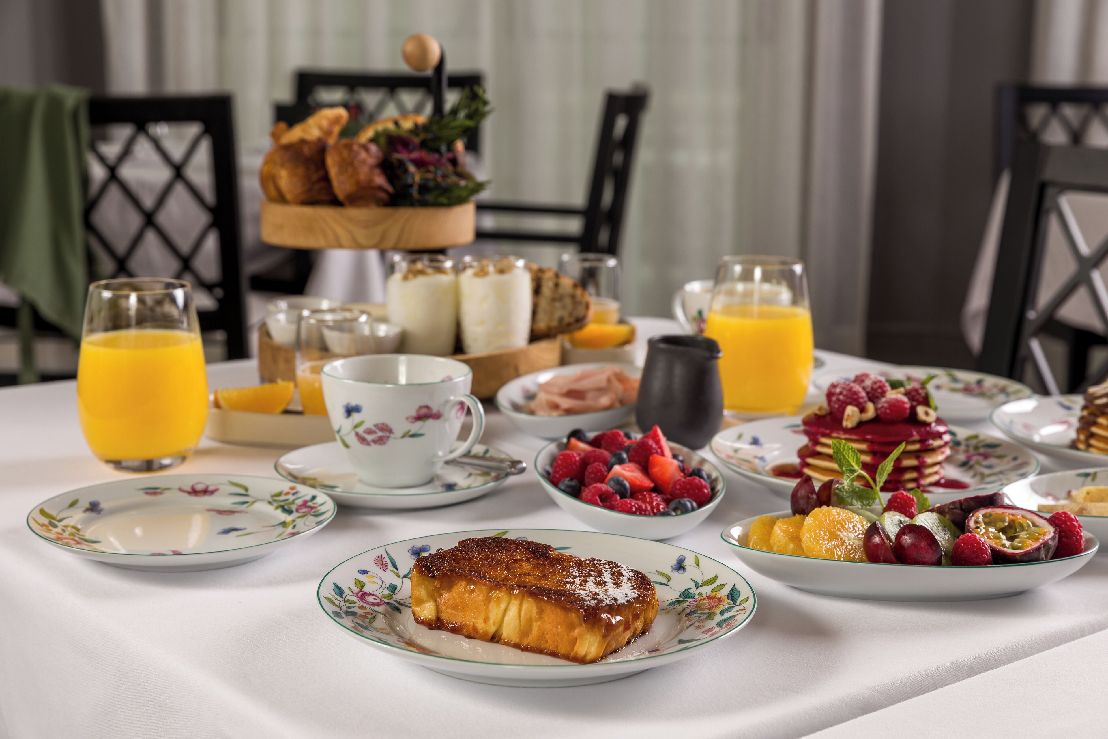 Uma mesa de café da manhã com diversos pratos, incluindo panquecas, frutas e suco.
