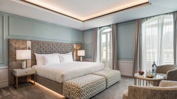 Quarto de hotel com uma cama grande, luminárias de cabeceira, uma mesinha com uma garrafa e uma cadeira.