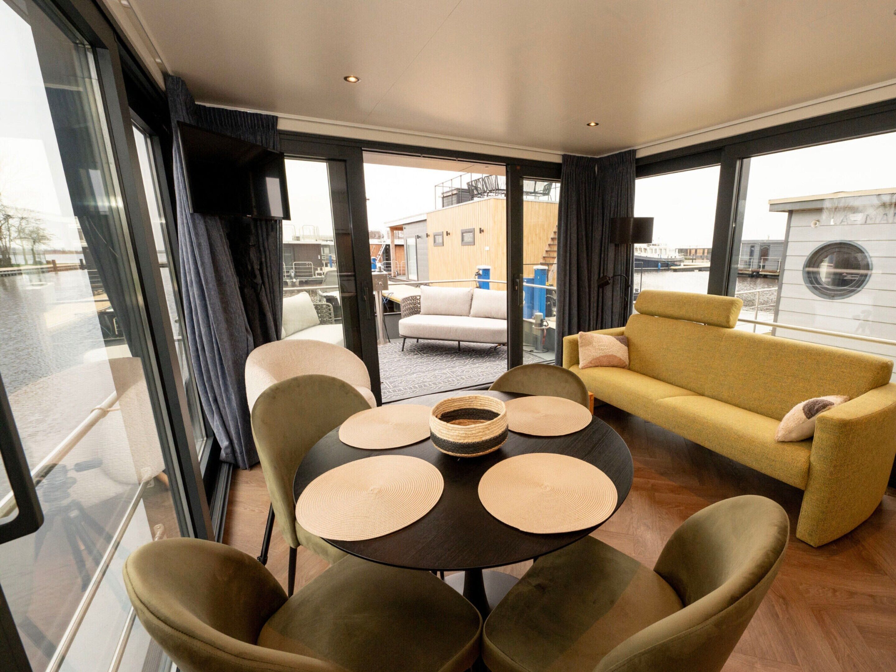 Quarto moderno com uma mesa redonda, quatro cadeiras, um sofá e grandes janelas com vista para a cidade.