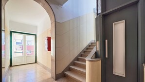 Escadaria que leva a uma porta escura, piso de azulejos e porta de vidro que dá para uma área externa.