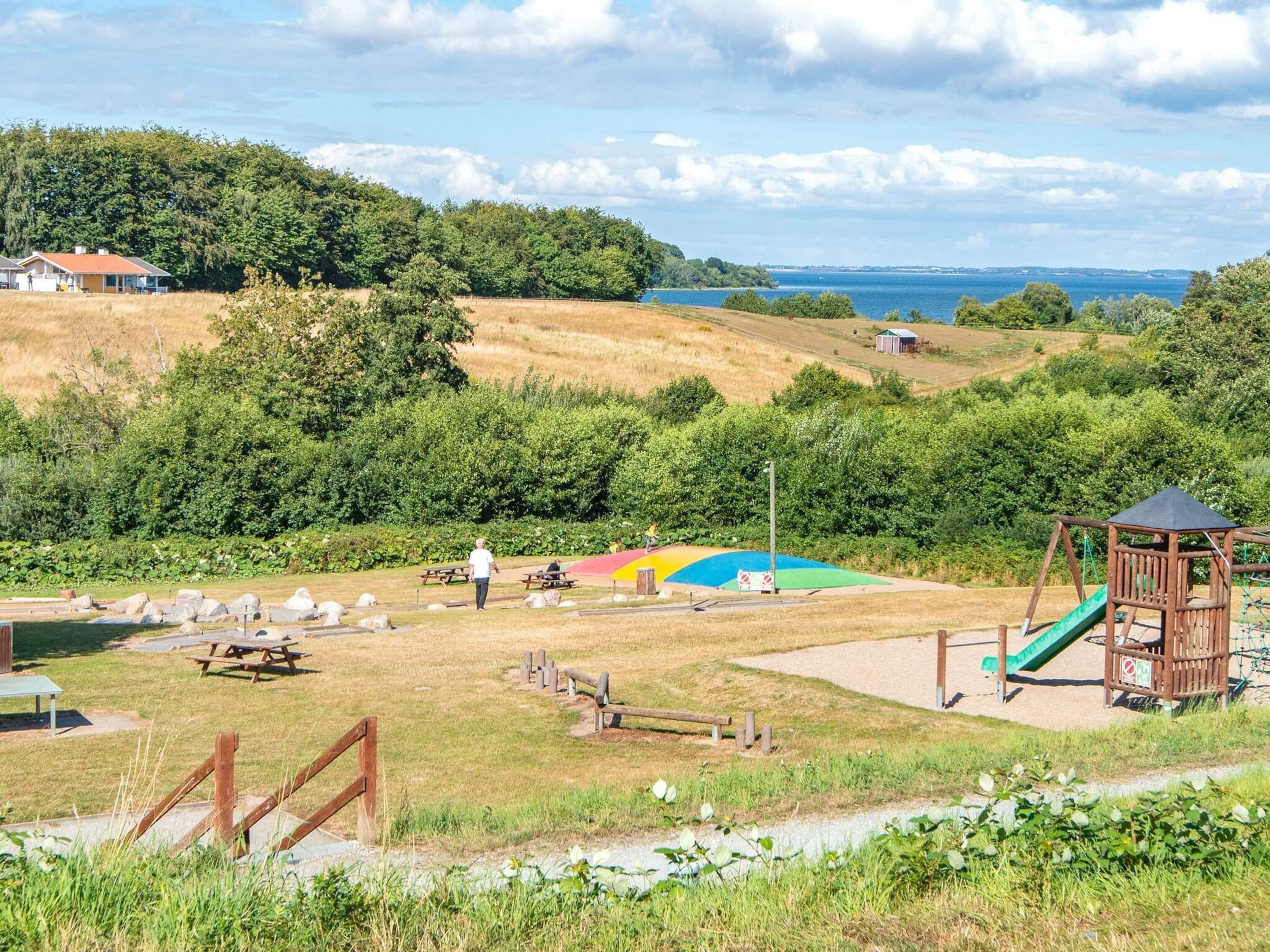 Um parque com mesas de piquenique, parquinho infantil e vista para o mar.