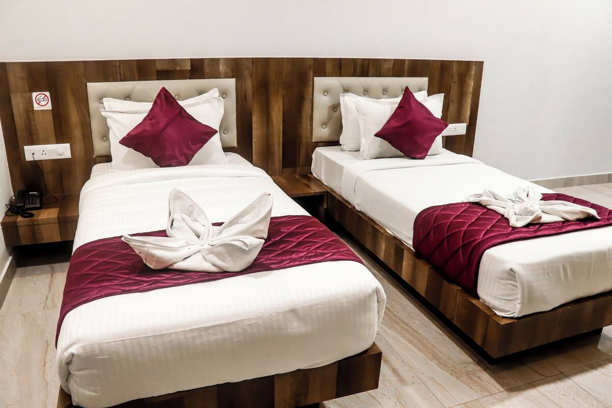 Quarto de hotel com duas camas, cada uma com cabeceira de madeira, roupa de cama branca e manta vermelha. Há um aviso de proibido fumar na parede e um telefone na mesa de cabeceira.