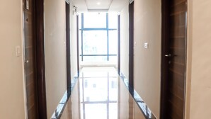 Um corredor comprido e estreito com piso brilhante e reflexivo, e portas escuras em ambos os lados.