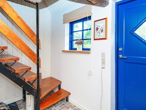 Uma escadaria com degraus de madeira e corrimãos pretos, uma porta azul, uma janela com vista para o verde e um quadro na parede.