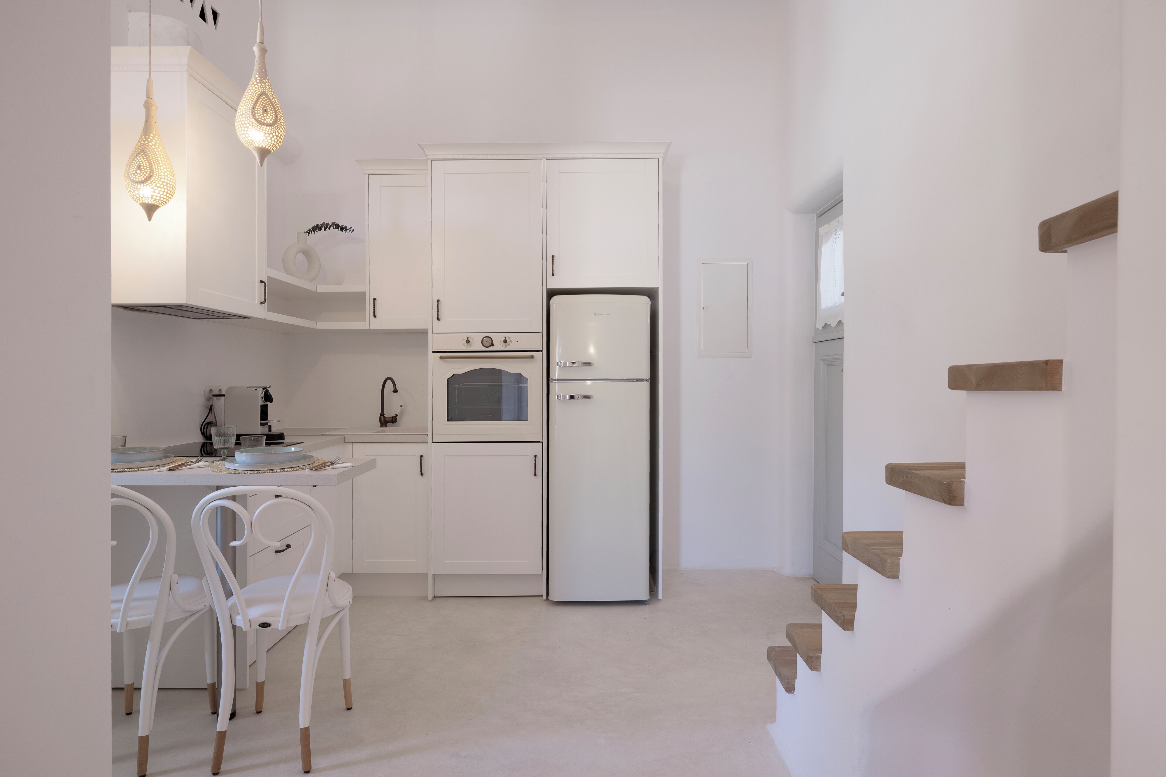 Cozinha moderna com armários brancos, geladeira e luminárias pendentes.