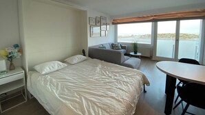 Quarto de hotel com cama, sofá, mesa de jantar e vista para a praia.