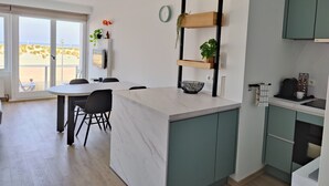 Cozinha moderna com bancada de mármore, armários verdes e vista para a praia.