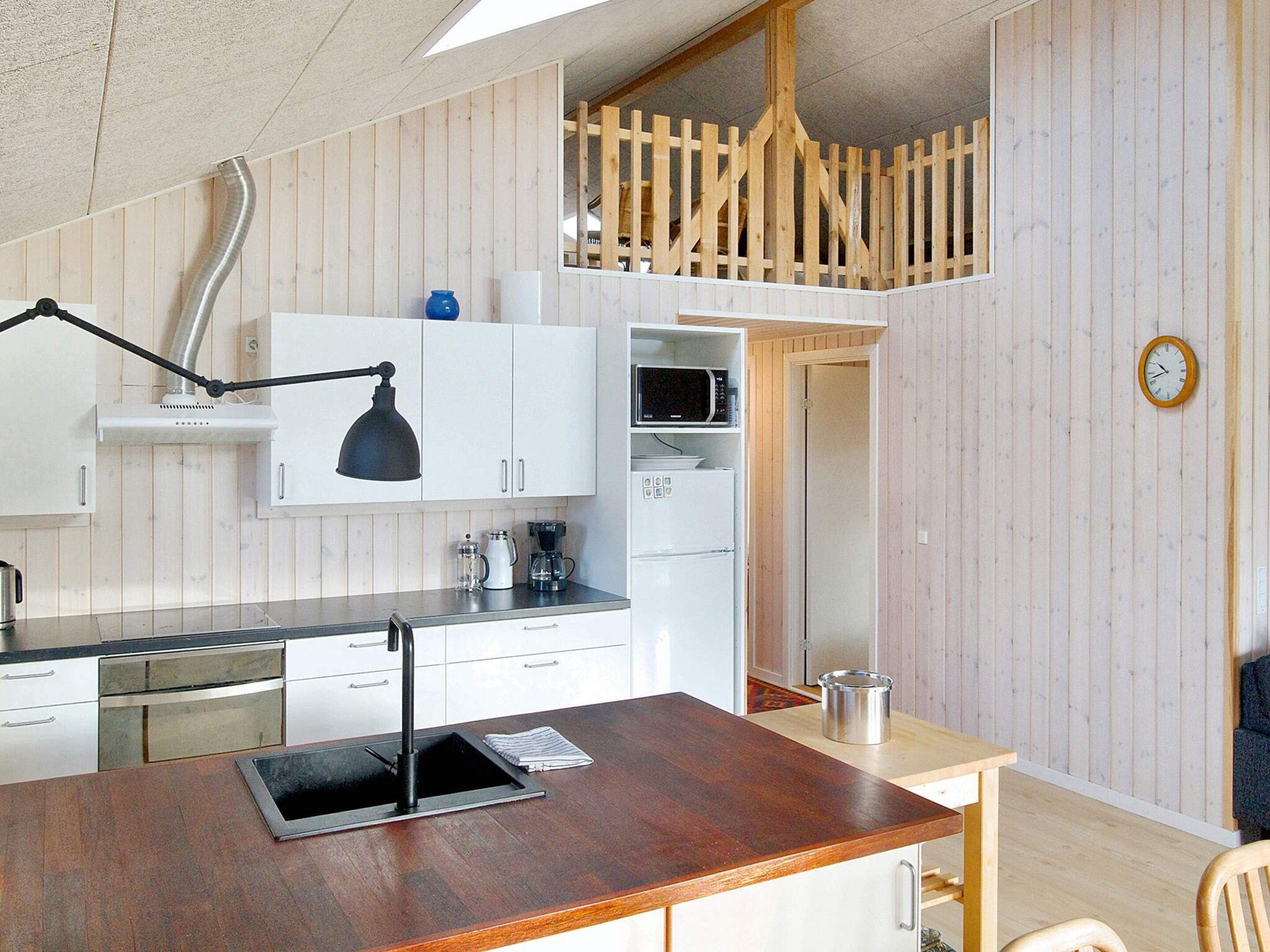 Cozinha compacta com armários brancos, uma mesa de jantar de madeira, uma luminária de mesa preta e um micro-ondas.