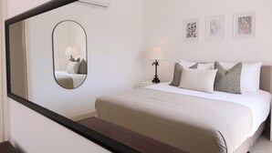Quarto com cama, mesa de cabeceira com abajur, espelho e três quadros na parede.
