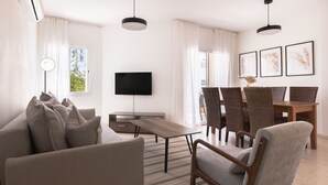 Uma sala de estar moderna com um sofá, uma televisão, uma mesa de jantar com cadeiras e uma janela grande com cortinas.
