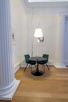 Quarto com uma mesa redonda, duas cadeiras, um abajur e uma obra de arte emoldurada na parede.