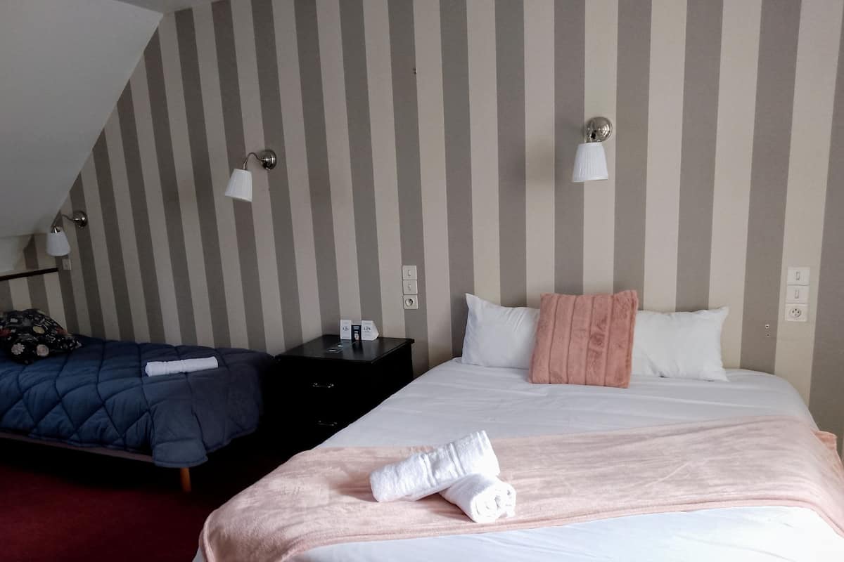 Quarto de hotel com uma cama, uma cama adicional, uma mesinha de cabeceira, um abajur e uma parede listrada.