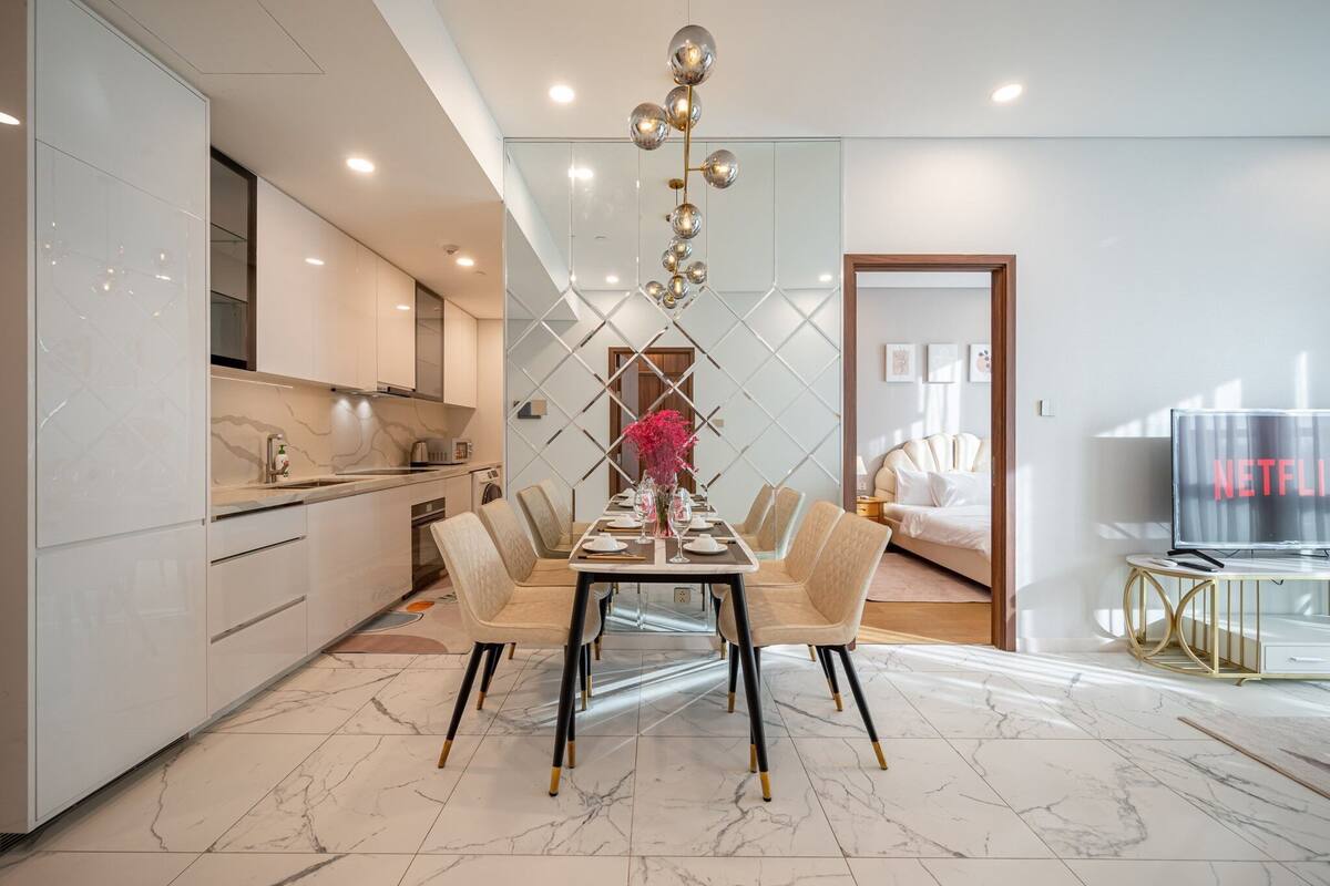 Uma cozinha moderna com área de jantar, apresentando piso de mármore, mesa de jantar com cadeiras e um lustre.
