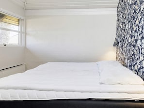 Cama bem arrumada com roupa de cama branca em quarto com paredes brancas e janela.