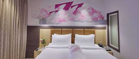 Quarto de hotel com uma cama grande, cabeceira com luminária e mesa de cabeceira com um vaso de flores, além de uma parede com um mural de nuvens.