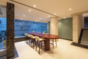 Uma sala de jantar moderna com uma mesa comprida e cadeiras, uma janela grande com vista para a cidade e uma escada que leva a um andar superior.