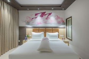 Quarto de hotel com cama grande, cabeceira com iluminação integrada, mesa de cabeceira com um vaso de flores e parede com painel floral.
