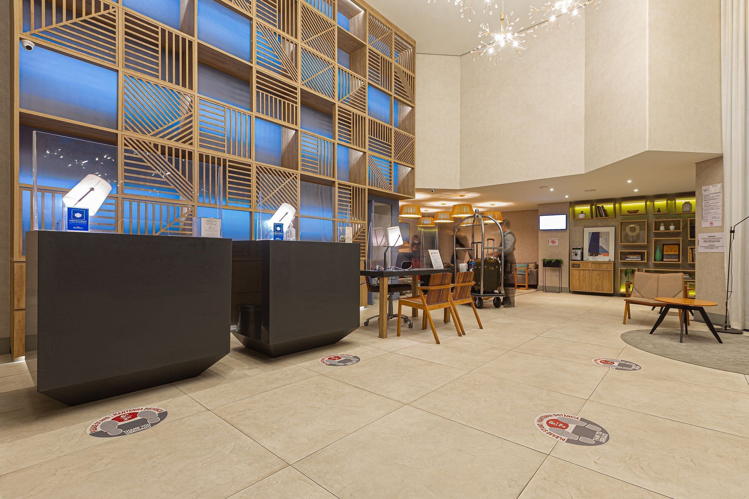 Um saguão de hotel com balcão de recepção, área de estar e uma parede decorativa com padrões geométricos.