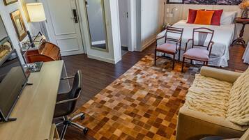 Quarto de hotel com uma mesa, cadeiras, cama, tapete xadrez e um quadro na parede.