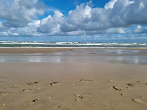 Uma praia com pegadas e ondas ao fundo.