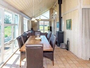 Uma sala de jantar com uma mesa de madeira comprida, várias cadeiras e uma grande janela com vista para o exterior.