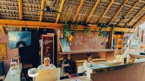 Balcão de recepção de um hostel, teto de madeira, placa com a inscrição 'VIAJERO HOSTELS' e um computador.