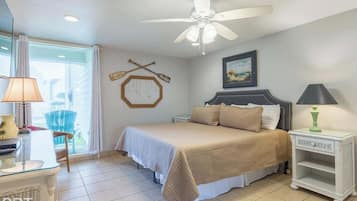 Quarto com cama, ventoinha no teto, mesa de cabeceira e janela com cortinas.