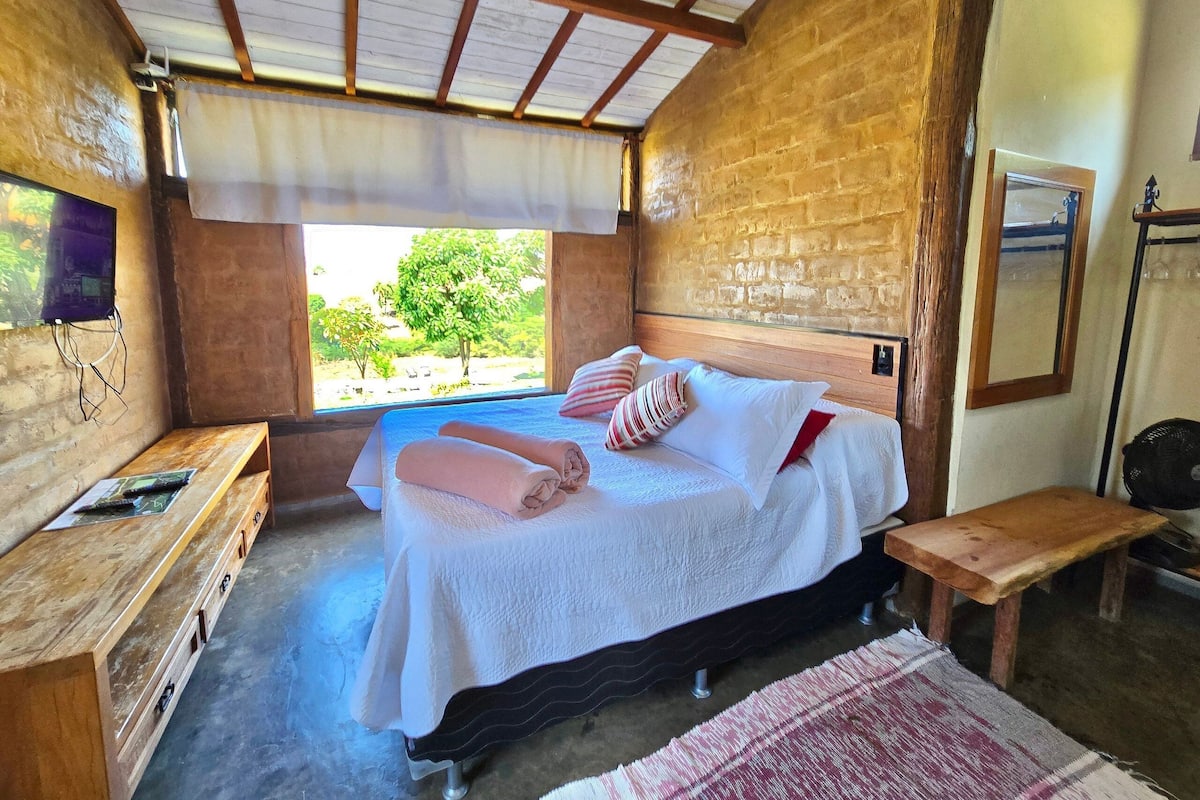 Quarto com cama, mesas de cabeceira, janela com vista e parede de tijolos.