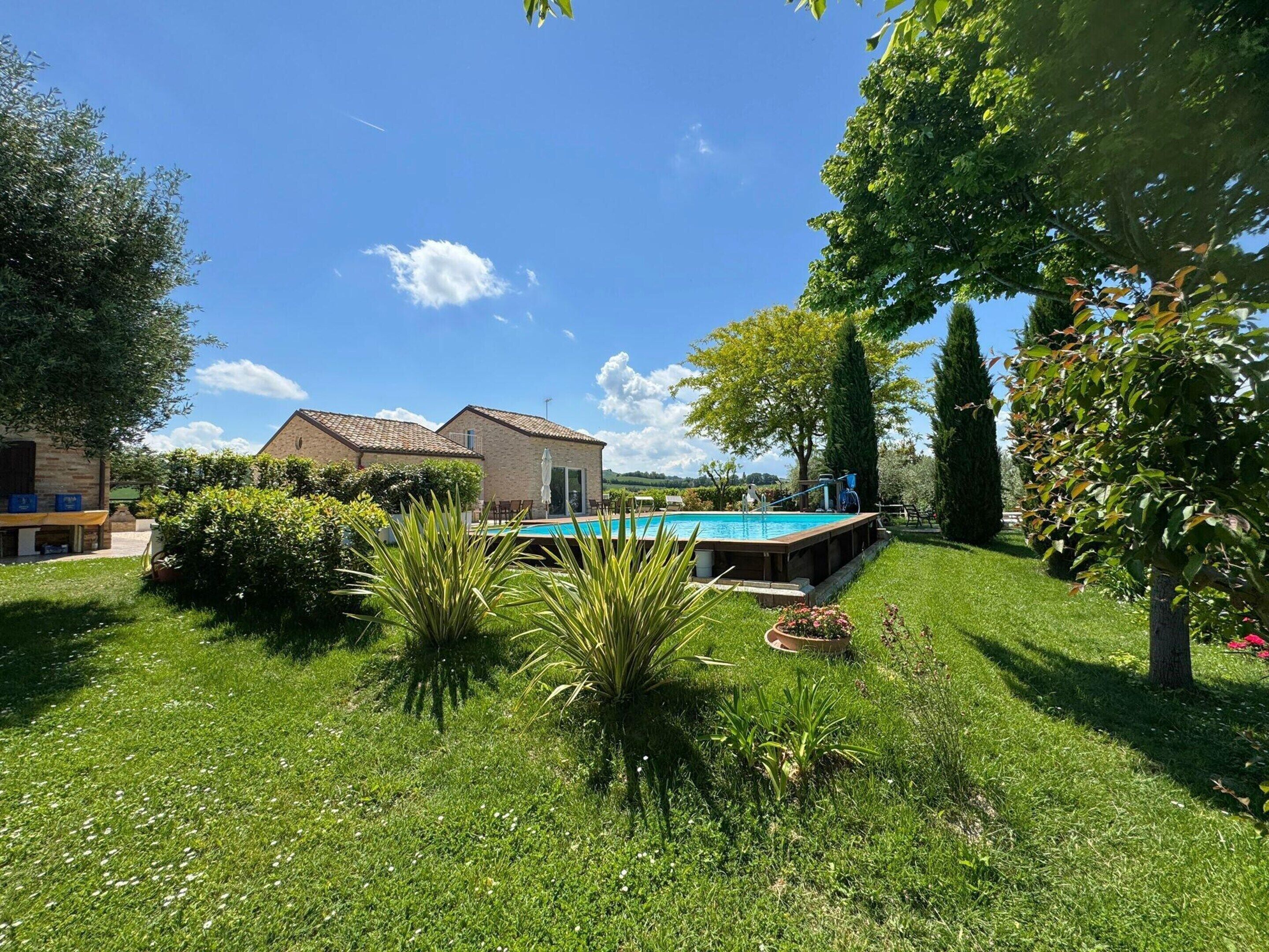 Um imóvel residencial com piscina, vegetação exuberante e céu azul límpido.