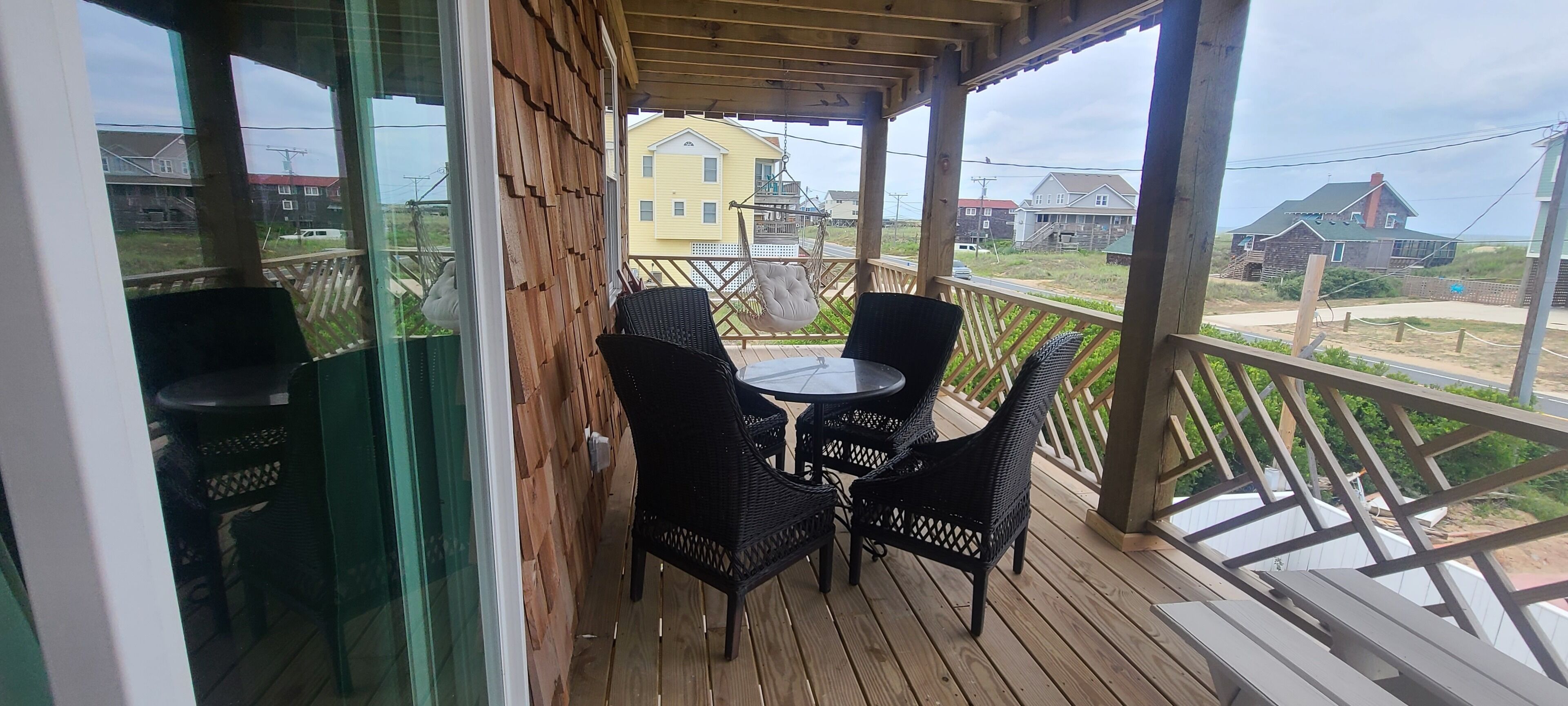 Uma área externa coberta com uma mesa e quatro cadeiras, um deck de madeira e vista para casas ao fundo.