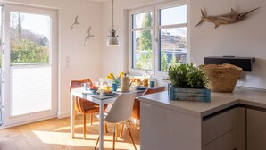 Uma cozinha luminosa com uma mesa de jantar, cadeiras, uma luminária pendente e uma janela grande.