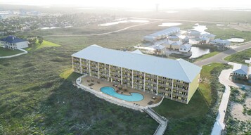Um grande hotel com várias varandas, uma piscina e cercado por corpos d'água e vegetação.
