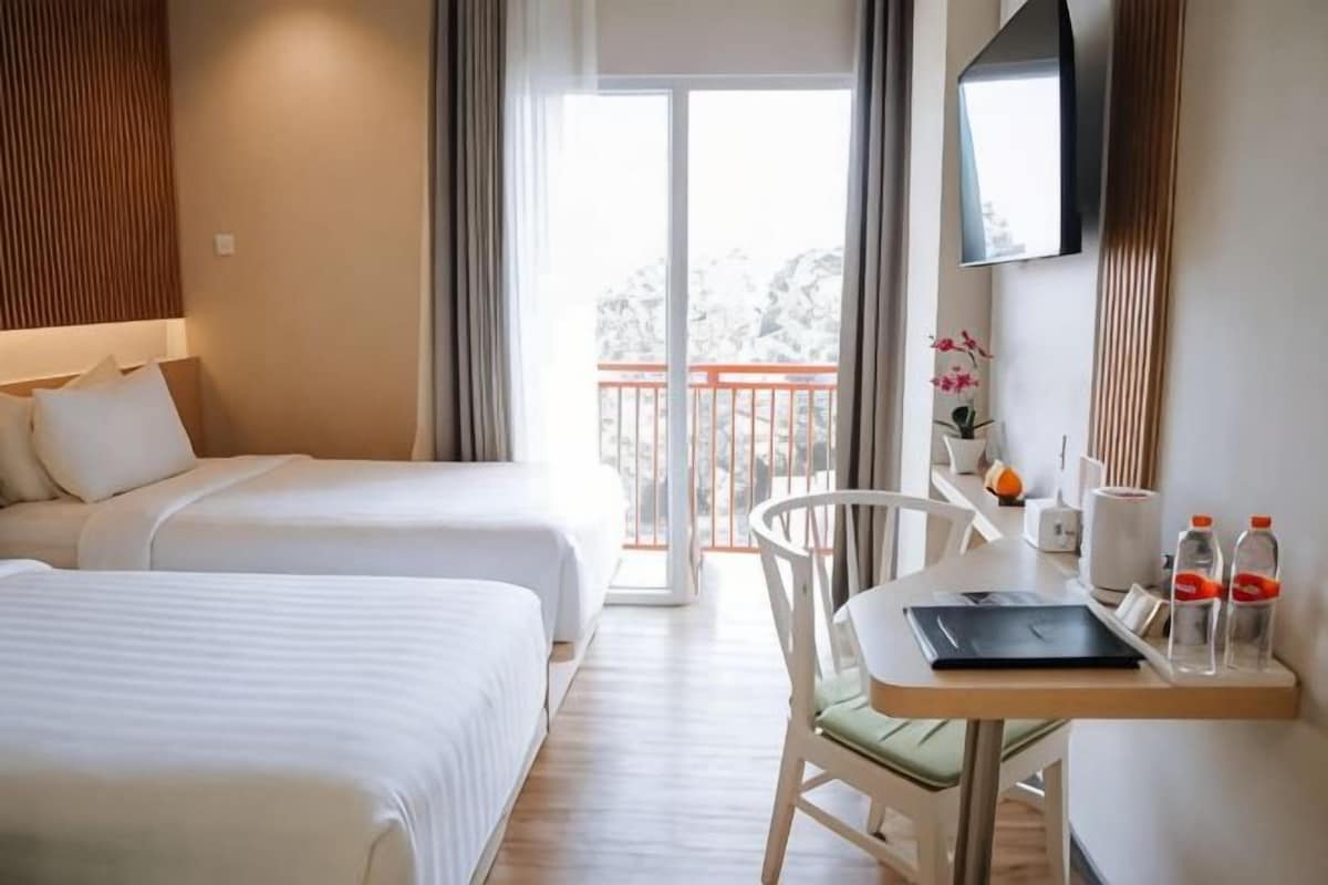 Quarto de hotel com duas camas, uma mesa com cadeira, televisão e varanda com vista.