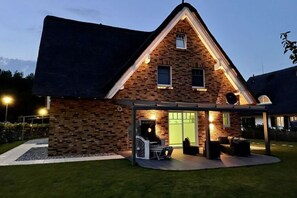 Uma casa moderna com fachada de tijolos, um alpendre coberto com móveis de jardim e uma porta verde.