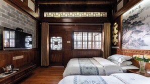 Quarto tradicional com paredes de madeira, uma parede de tijolos, uma TV, uma cama com roupa de cama estampada, uma escrivaninha com um bule e um quadro na parede.