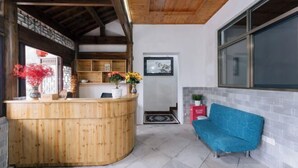 Uma área de recepção com balcão de madeira, sofá azul e piso ladrilhado.