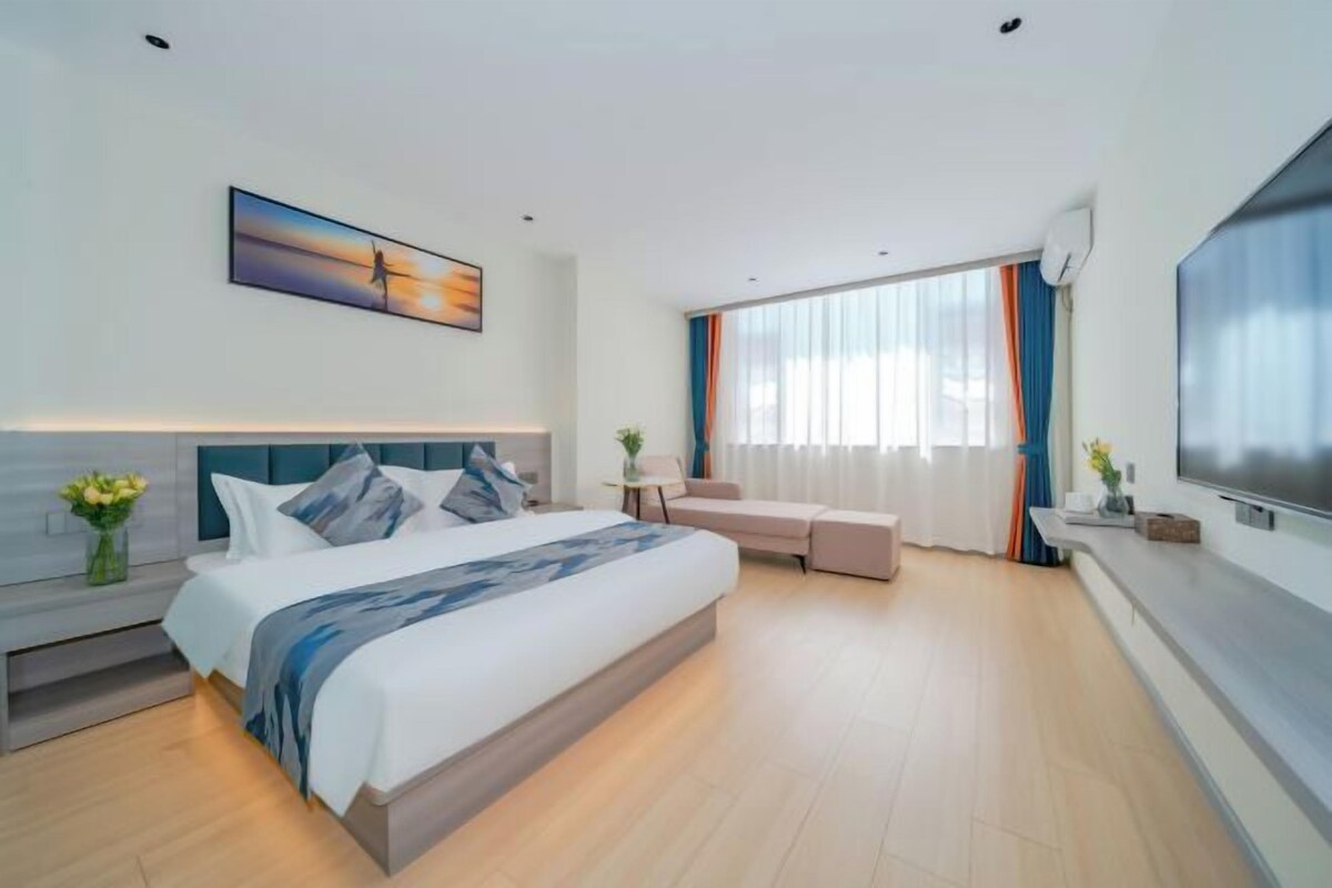 Quarto de hotel moderno com uma cama grande, televisão, sofá e janela com cortinas.