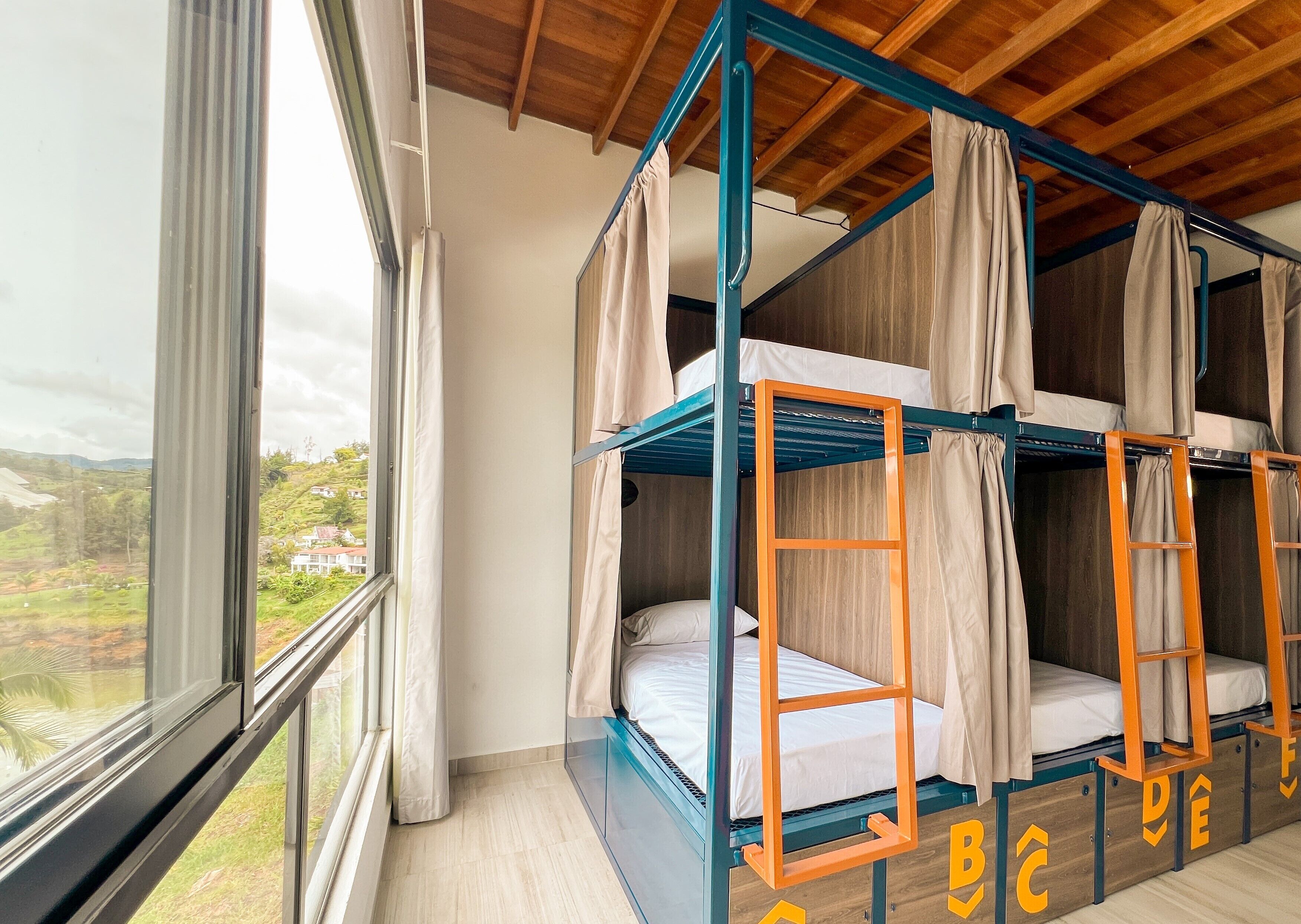 Quarto com beliches, uma janela grande e vista para uma paisagem verde.