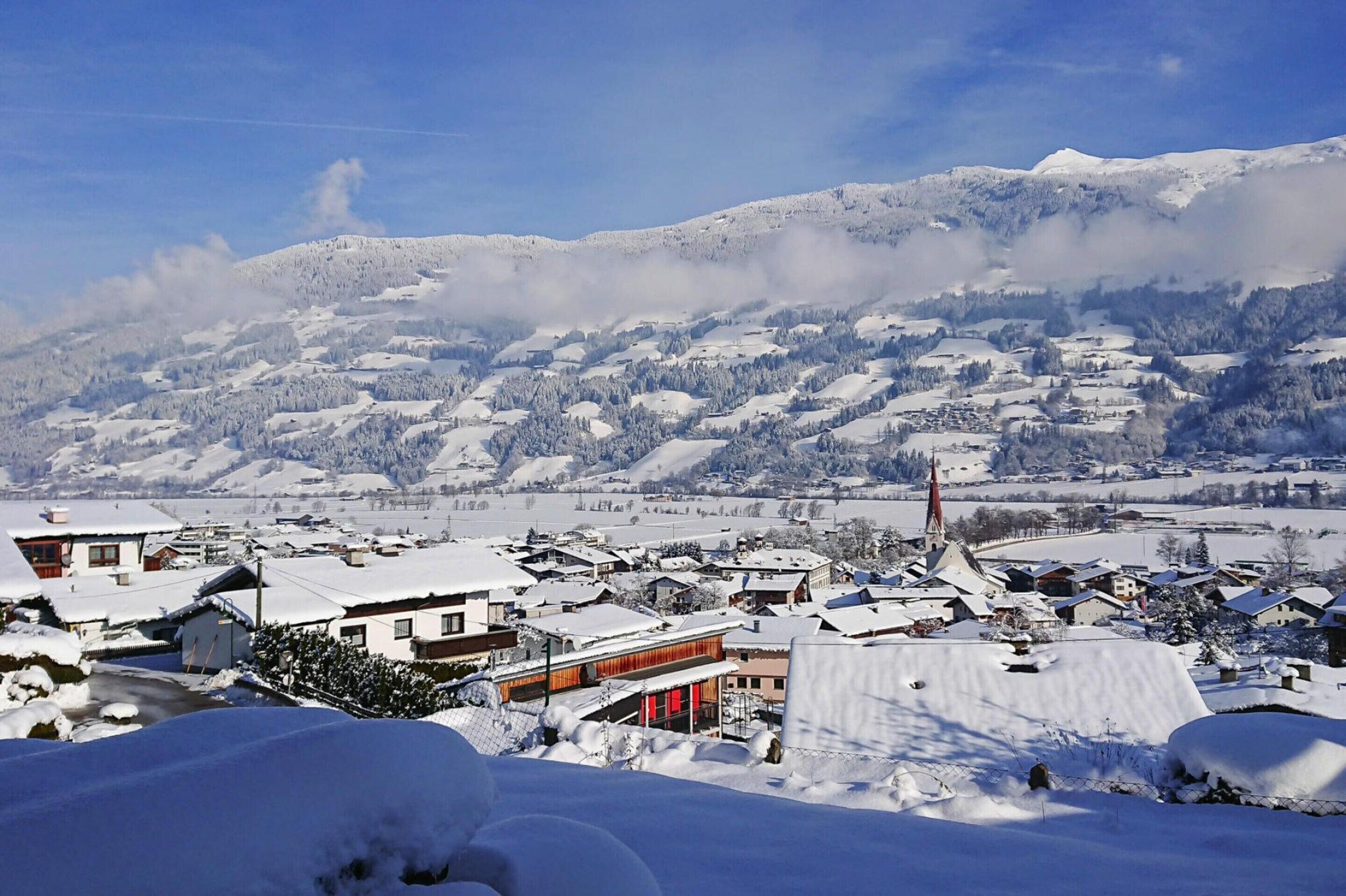 Uma aldeia coberta de neve, com casas e uma igreja, rodeada por montanhas.